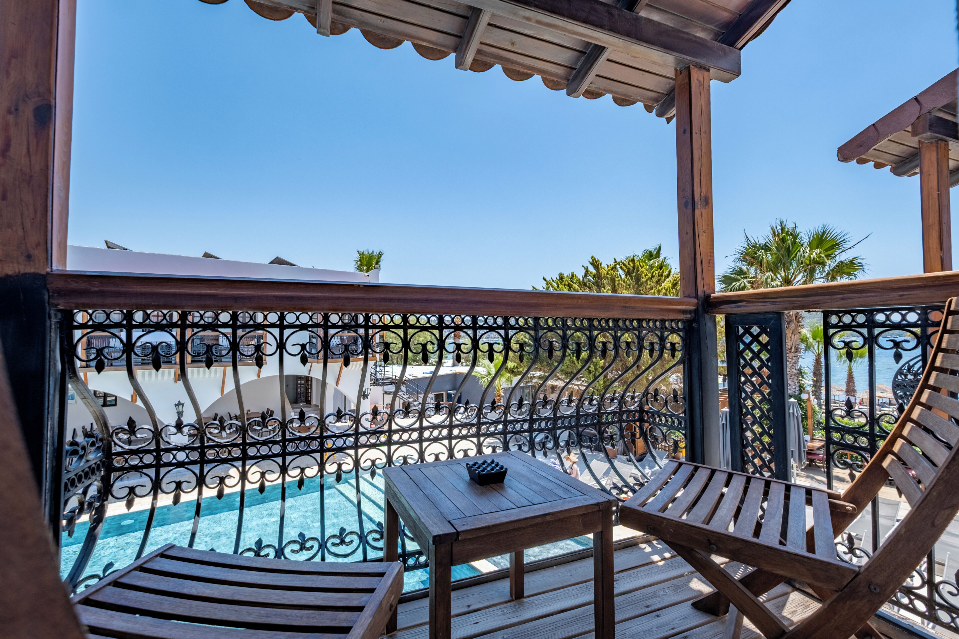 Um deck de madeira com piscina, guarda-corpo de metal e cadeiras de sol.