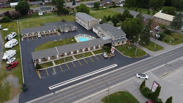 Vista aérea de um motel com piscina, várias vagas de estacionamento e uma estrada em primeiro plano.