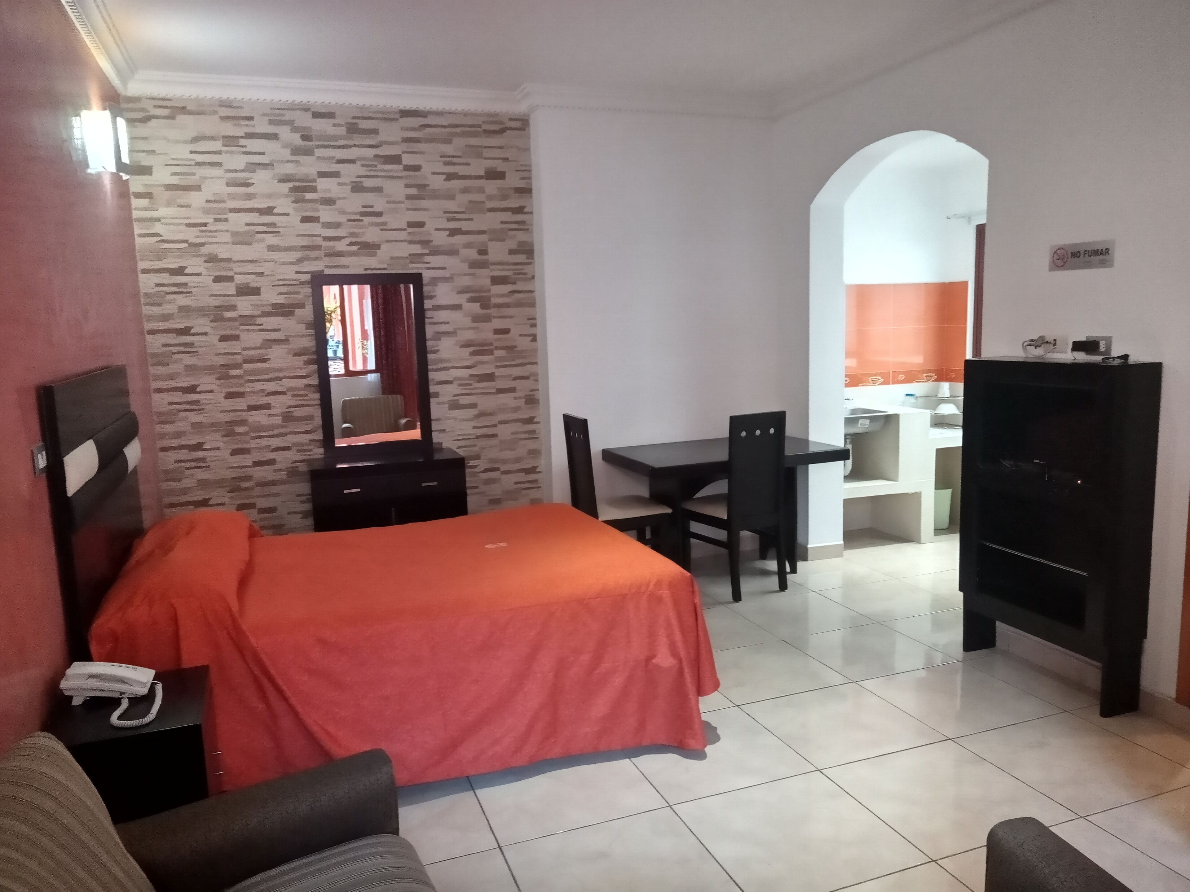 Quarto de hotel com cama, secretária, cadeira, guarda-roupa e casa de banho visível por um arco.