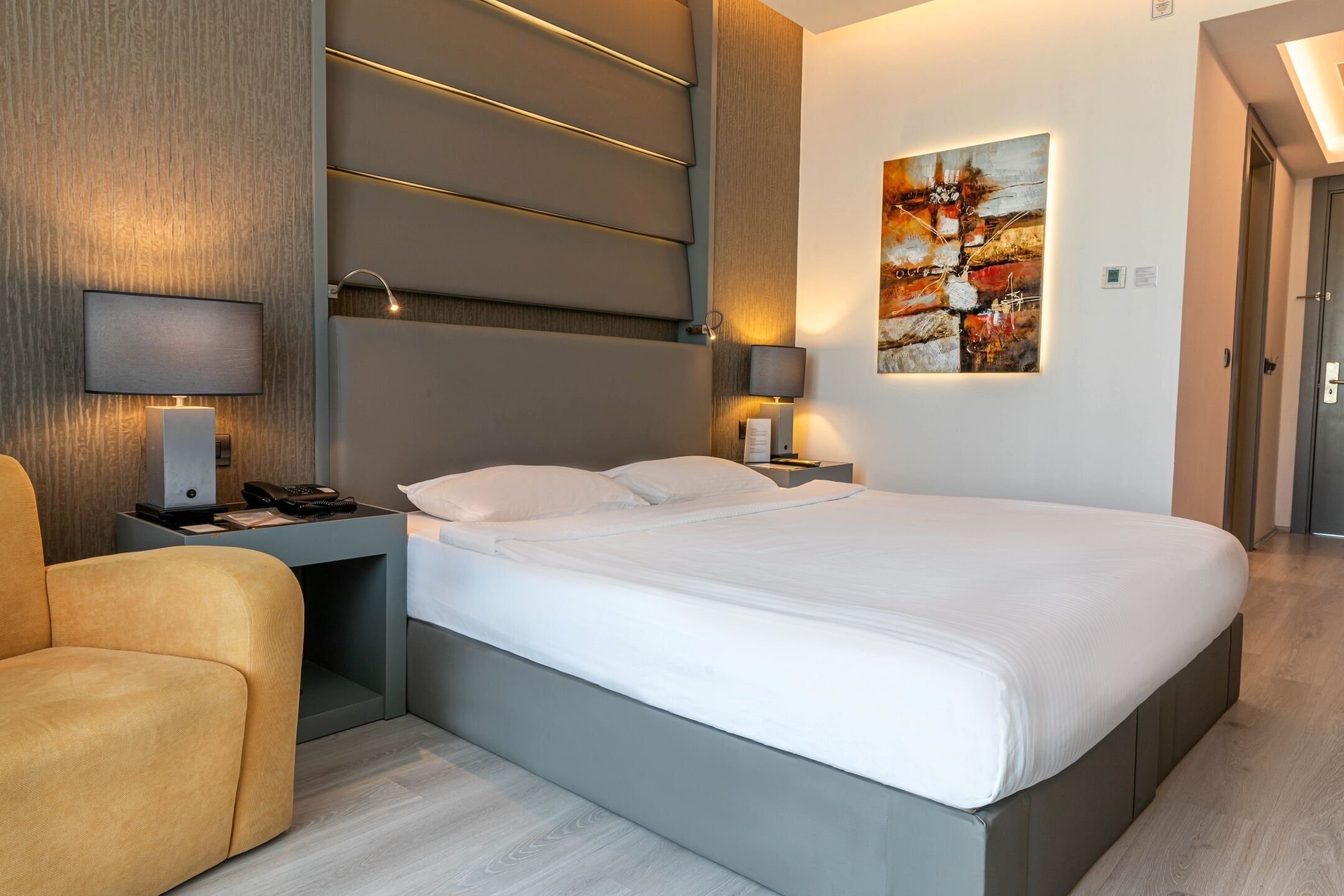 Quarto de hotel moderno com uma cama grande, mesas de cabeceira, escrivaninha e uma cadeira.