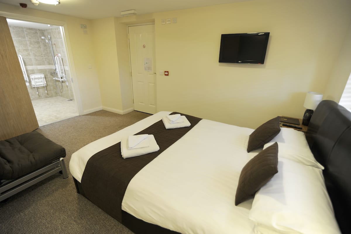 Quarto de hotel com cama, televisão, escrivaninha e área de chuveiro.