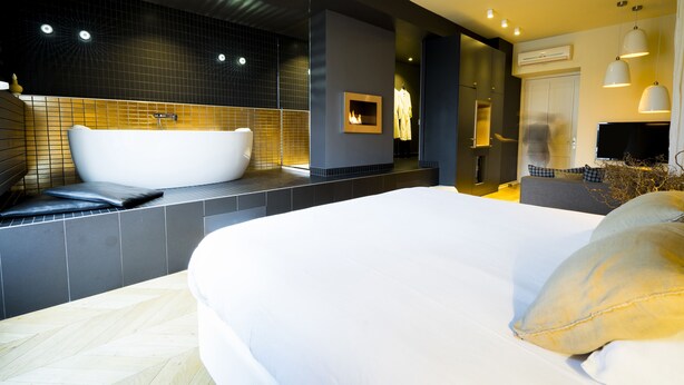 Quarto de hotel moderno com cama grande, banheira e área de chuveiro separada.