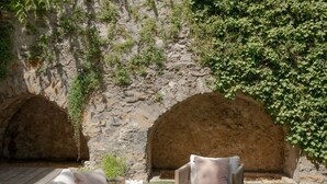 Um pátio com móveis de vime, parede de pedra e vegetação.