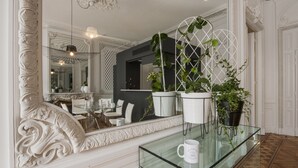 Um interior moderno com mesa de centro de vidro, molduras decorativas brancas e um espelho refletindo uma área de jantar.