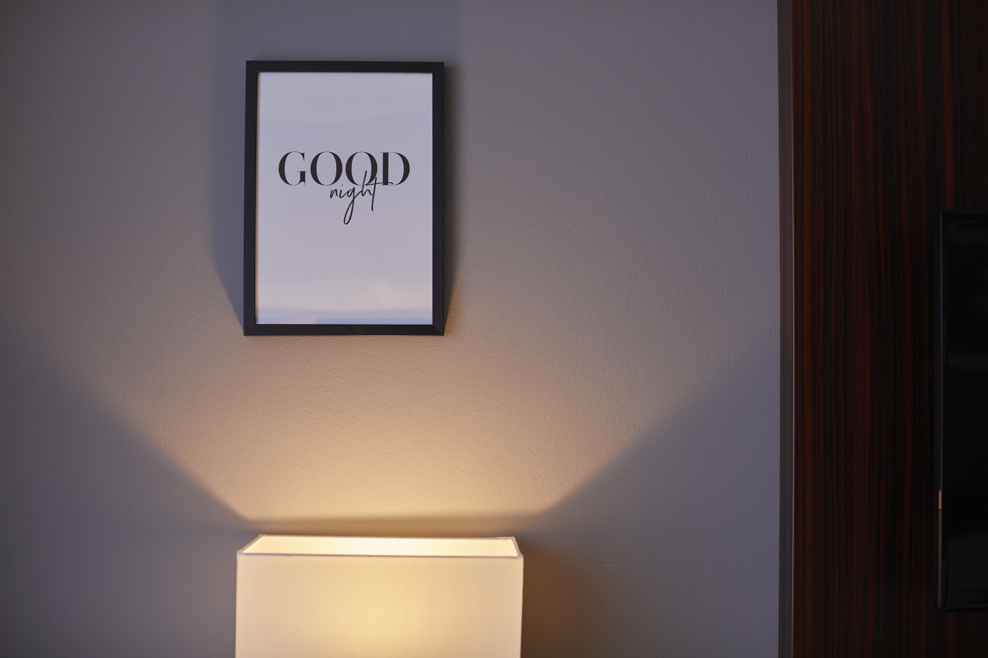 Um letreiro emoldurado com o texto 'GOOD night' numa parede, uma luminária presa à parede e um rodapé de porta de madeira.