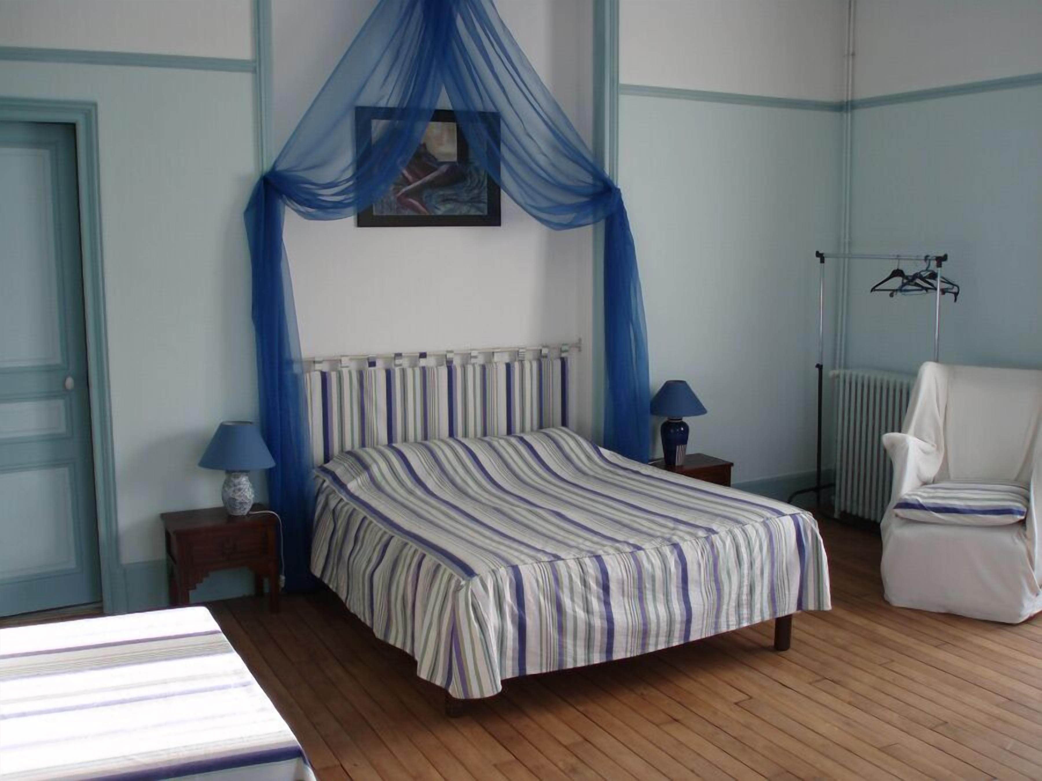 Um quarto com cama, luminárias de cabeceira, uma cadeira e um radiador.
