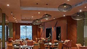 Uma sala de jantar moderna com piso de madeira, várias mesas e cadeiras, e luminárias decorativas pendentes.
