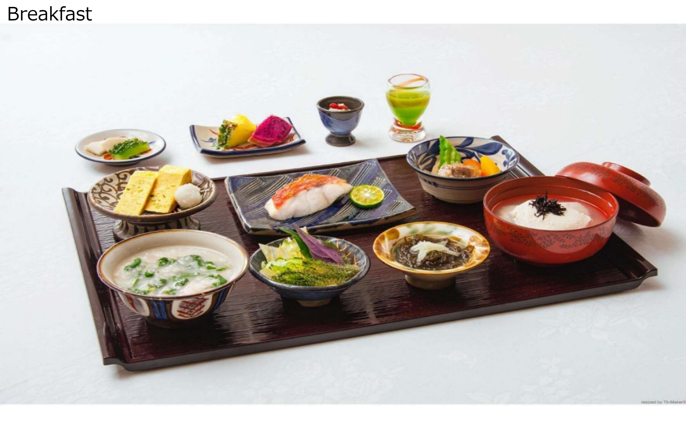 Um café da manhã tradicional japonês disposto em uma bandeja, incluindo diversos pratos como sushi, vegetais em conserva e uma bebida de chá verde.
