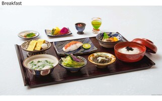 Um café da manhã tradicional japonês disposto em uma bandeja, incluindo diversos pratos como sushi, vegetais em conserva e uma bebida de chá verde.