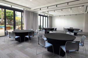 Uma sala de conferências com mesas e cadeiras redondas, amplas janelas e vista para o exterior.