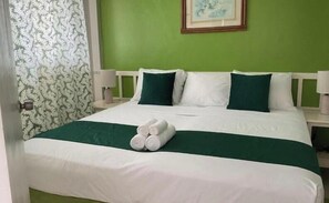 Cama bem arrumada com lençóis brancos e verdes, um par de toalhas enroladas e um quadro na parede.