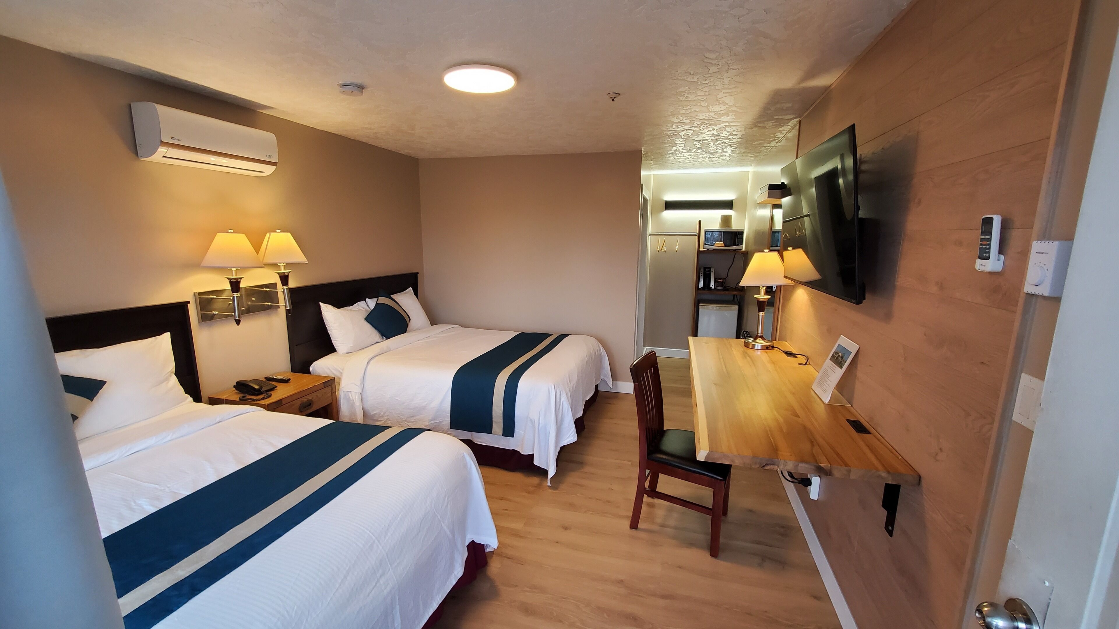 Quarto de hotel com duas camas, uma escrivaninha, uma cadeira, televisão e micro-ondas.