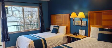 Quarto de hotel com duas camas, uma janela com cortinas, uma cabeceira de madeira e uma mesa de cabeceira com abajur e telefone.