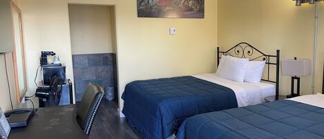 Quarto de hotel com duas camas, uma escrivaninha, uma cadeira, um abajur e um quadro na parede.