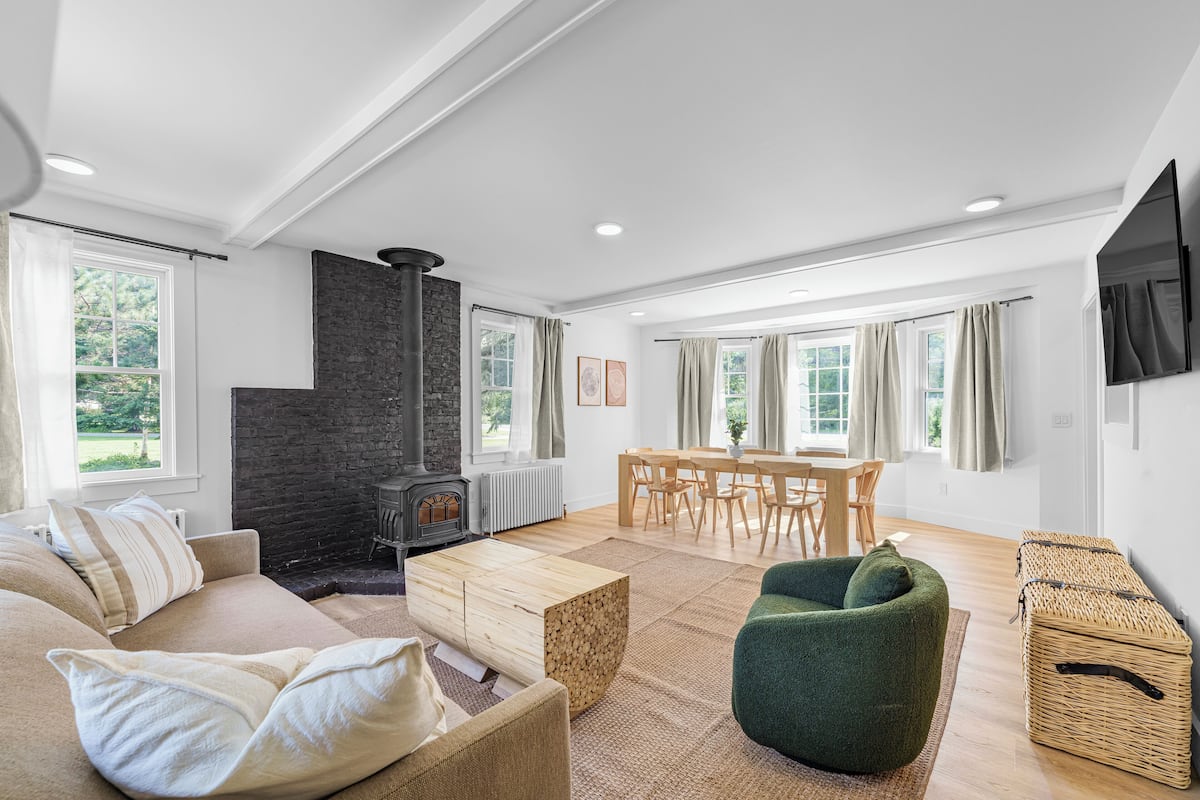 Uma sala de estar moderna com lareira, um sofá, uma poltrona verde, uma mesa de jantar e uma TV fixada na parede.