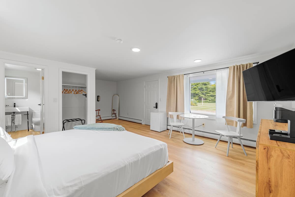 Quarto de hotel moderno com cama, escrivaninha, cadeira, televisão e janela com vista para o verde.