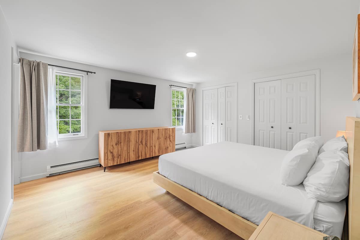 Quarto moderno com uma cama grande, móveis de madeira e uma TV fixada na parede.