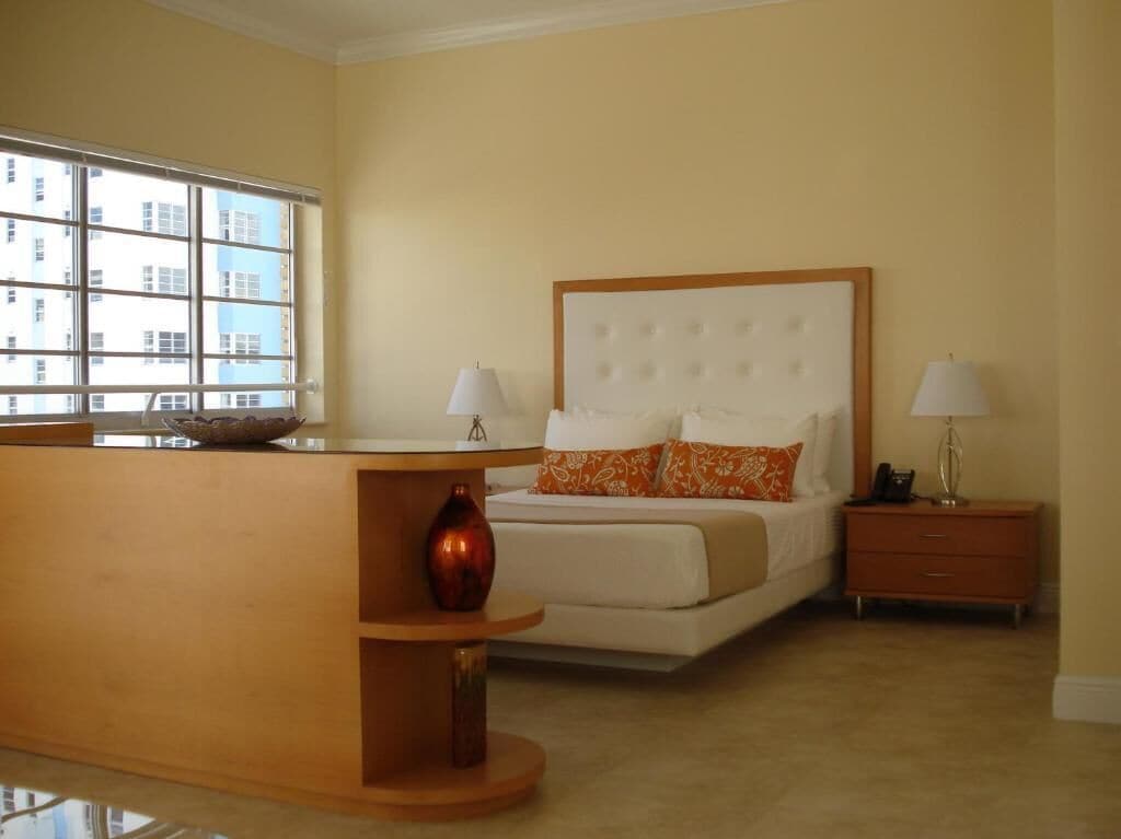 Quarto com cama, mesas de cabeceira, escrivaninha e área de trabalho.