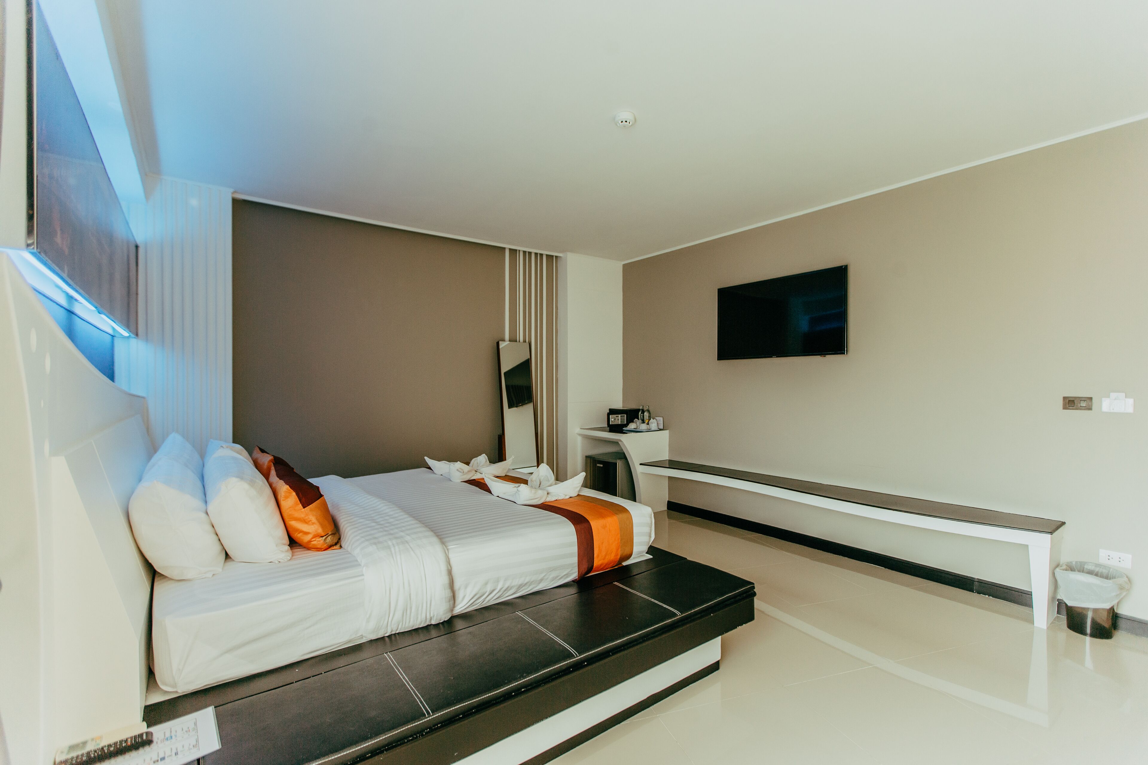 Quarto de hotel moderno com uma cama grande, uma televisão de tela plana na parede e uma pequena mesa com uma cadeira.