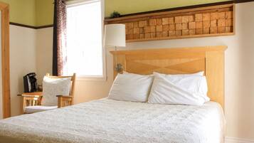 Quarto com cabeceira de madeira, cama com roupa de cama branca, mesa de cabeceira com abajur e janela com cortina.