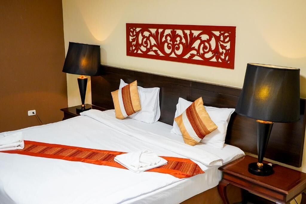 Quarto de hotel com uma cama grande, duas mesas de cabeceira, um ornamento na parede e duas luminárias.