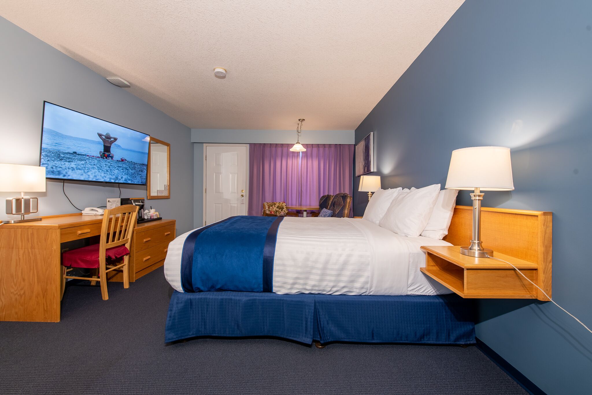 Quarto de hotel com cama, escrivaninha, cadeira, televisão e vista para o mar.