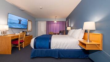 Quarto de hotel com cama, escrivaninha, cadeira, televisão e vista para o mar.