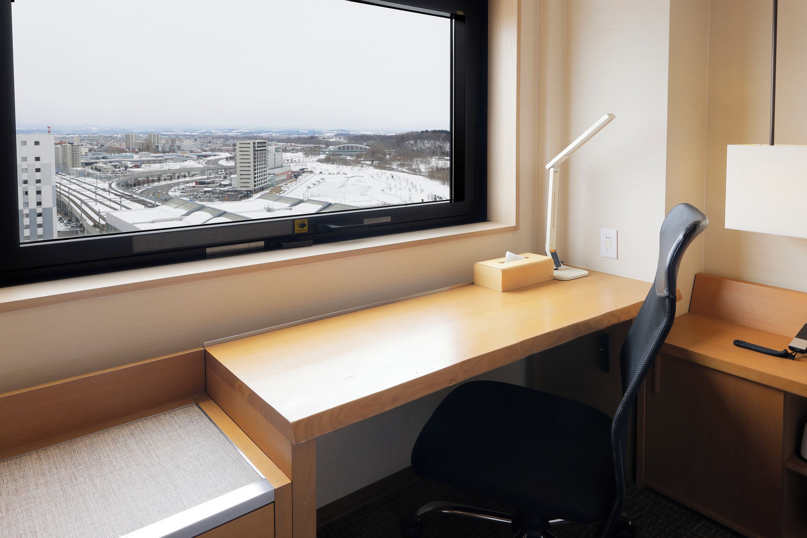 Um espaço de escritório moderno com uma janela grande, uma mesa, uma cadeira e uma luminária.