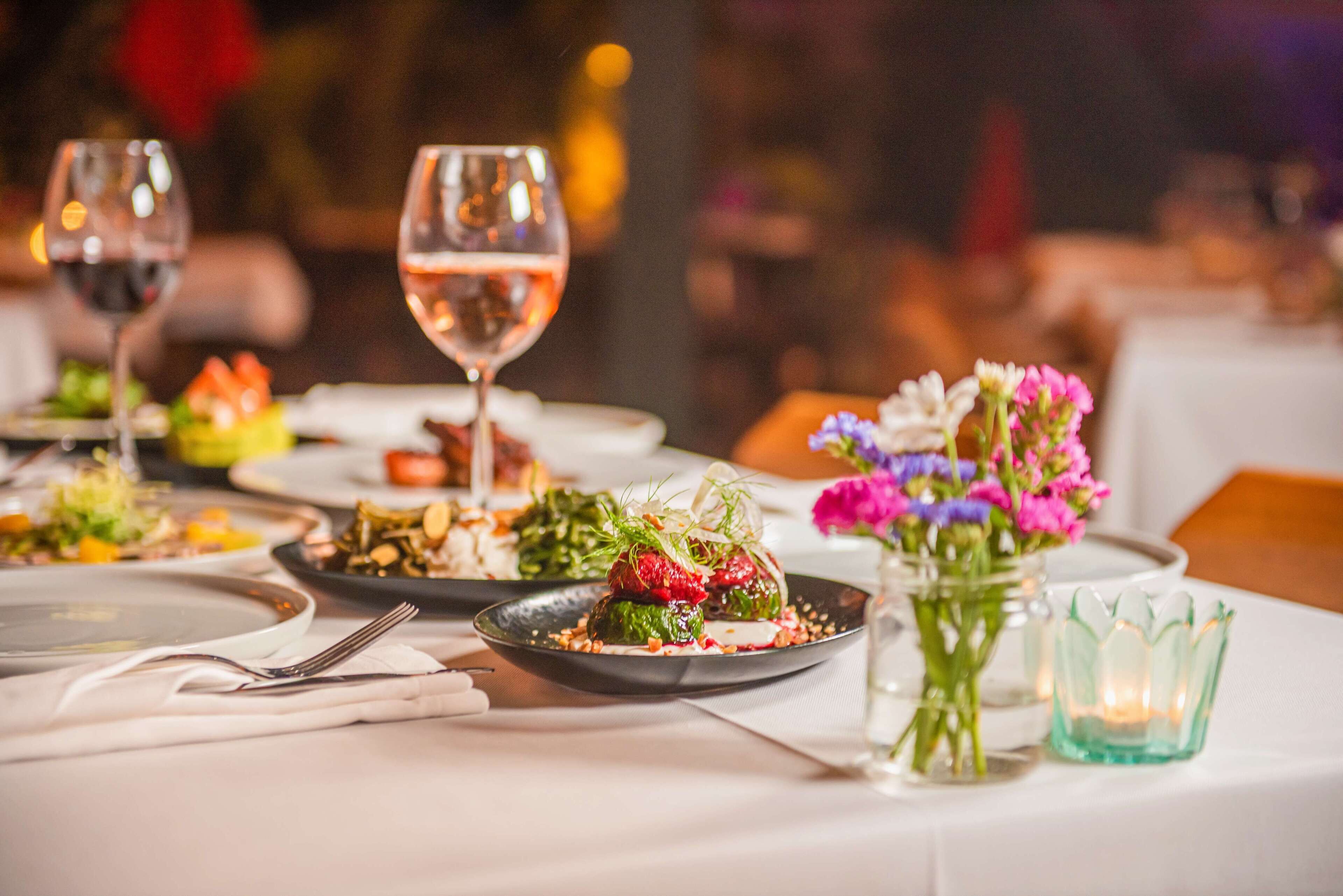 Uma mesa posta para refeição, com pratos, copos e um vaso de flores.