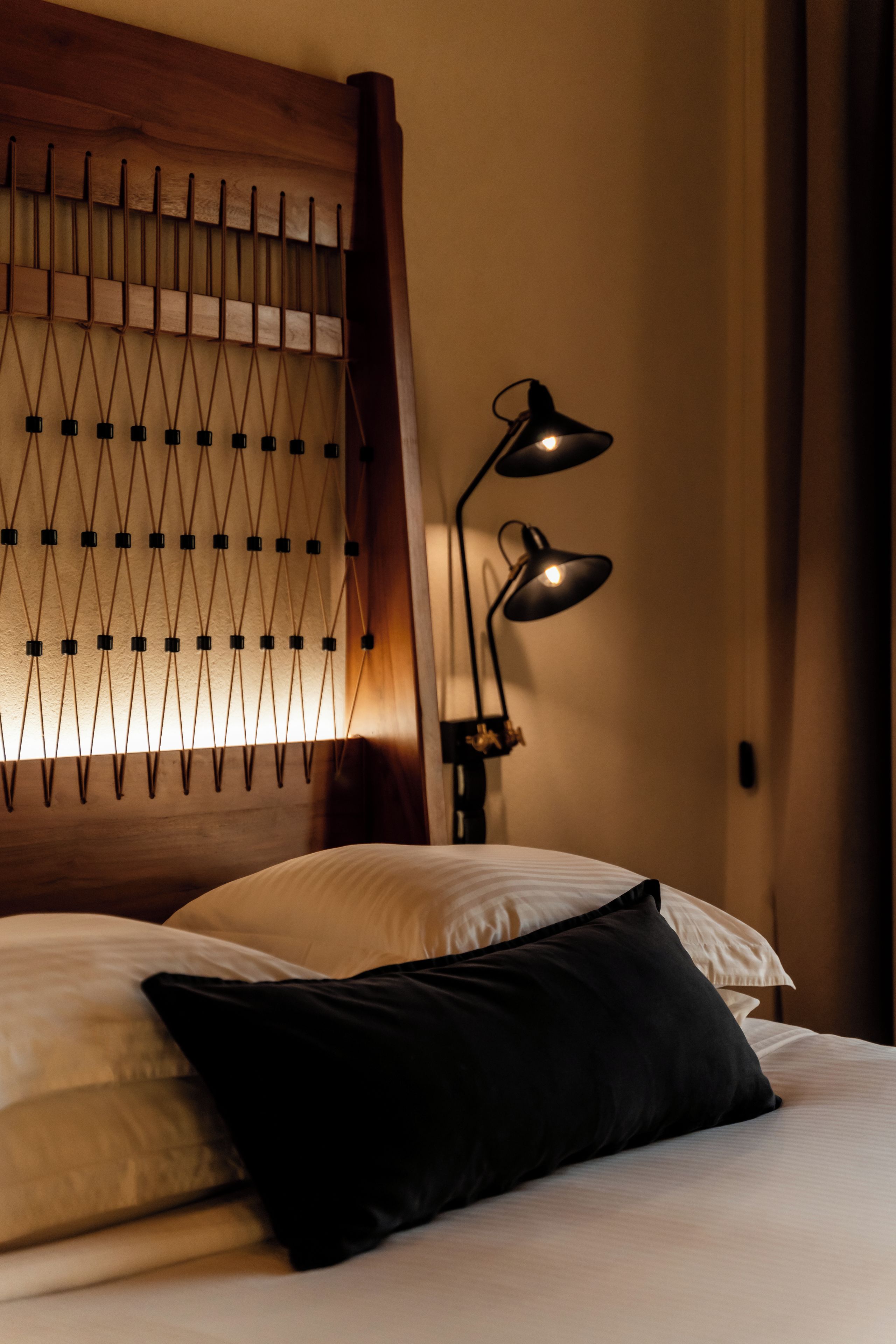 Cama bem arrumada com cabeceira de madeira e duas luminárias de cabeceira.
