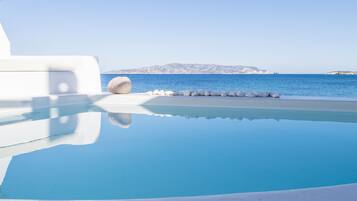 Piscina azul límpida com pedras brancas e um edifício branco, refletindo o céu e a água.