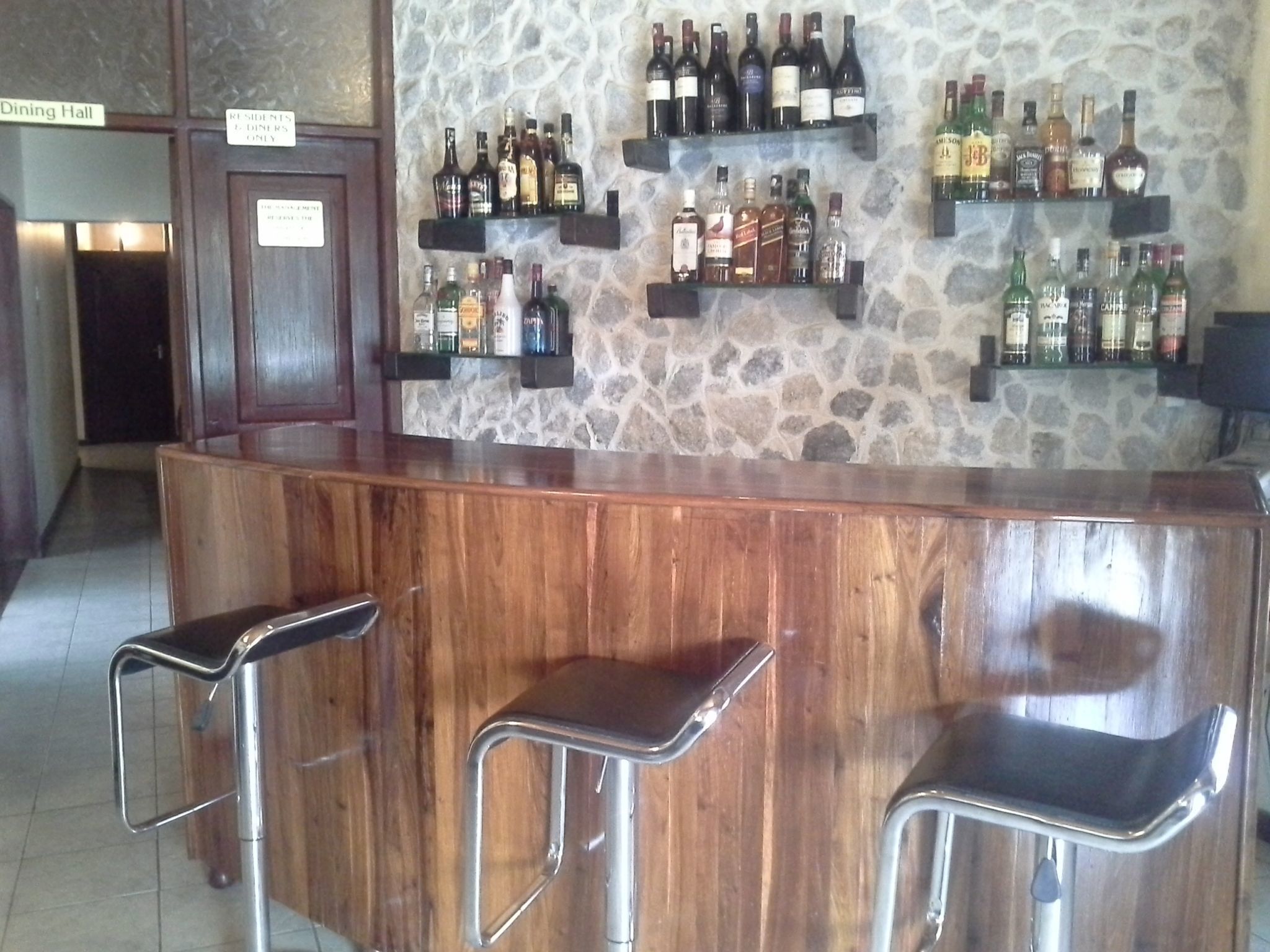 Uma área de bar com banquetas de madeira e prateleiras cheias de garrafas de bebidas.