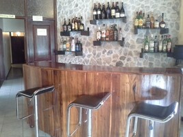 Uma área de bar com banquetas de madeira e prateleiras cheias de garrafas de bebidas.