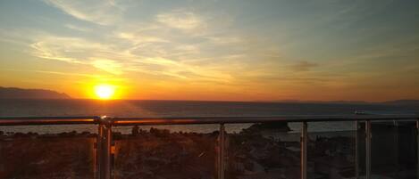 Vista do pôr do sol a partir de uma varanda com vista para a costa, com edifícios ao primeiro plano.
