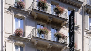 Um edifício de vários andares com varandas decoradas com caixas de flores. O edifício apresenta um estilo arquitetônico clássico com grades de ferro ornamentadas e uma placa indicando que é o New Orient Hotel.