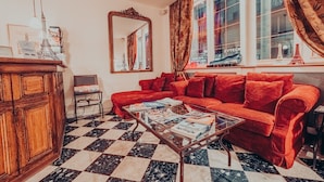 Uma sala de estar com piso xadrez, um sofá vermelho, um armário de madeira e uma mesa de centro de vidro.