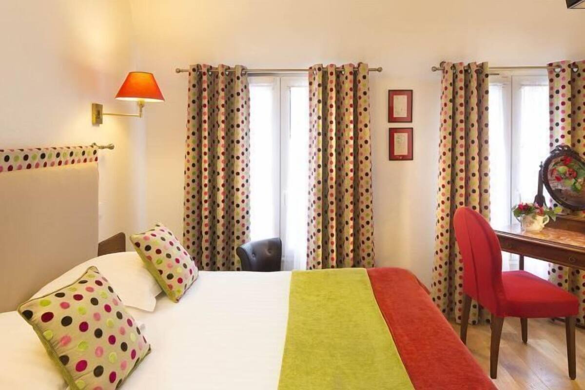 Quarto de hotel com cama, secretária, cadeira, cortinas e abajur.