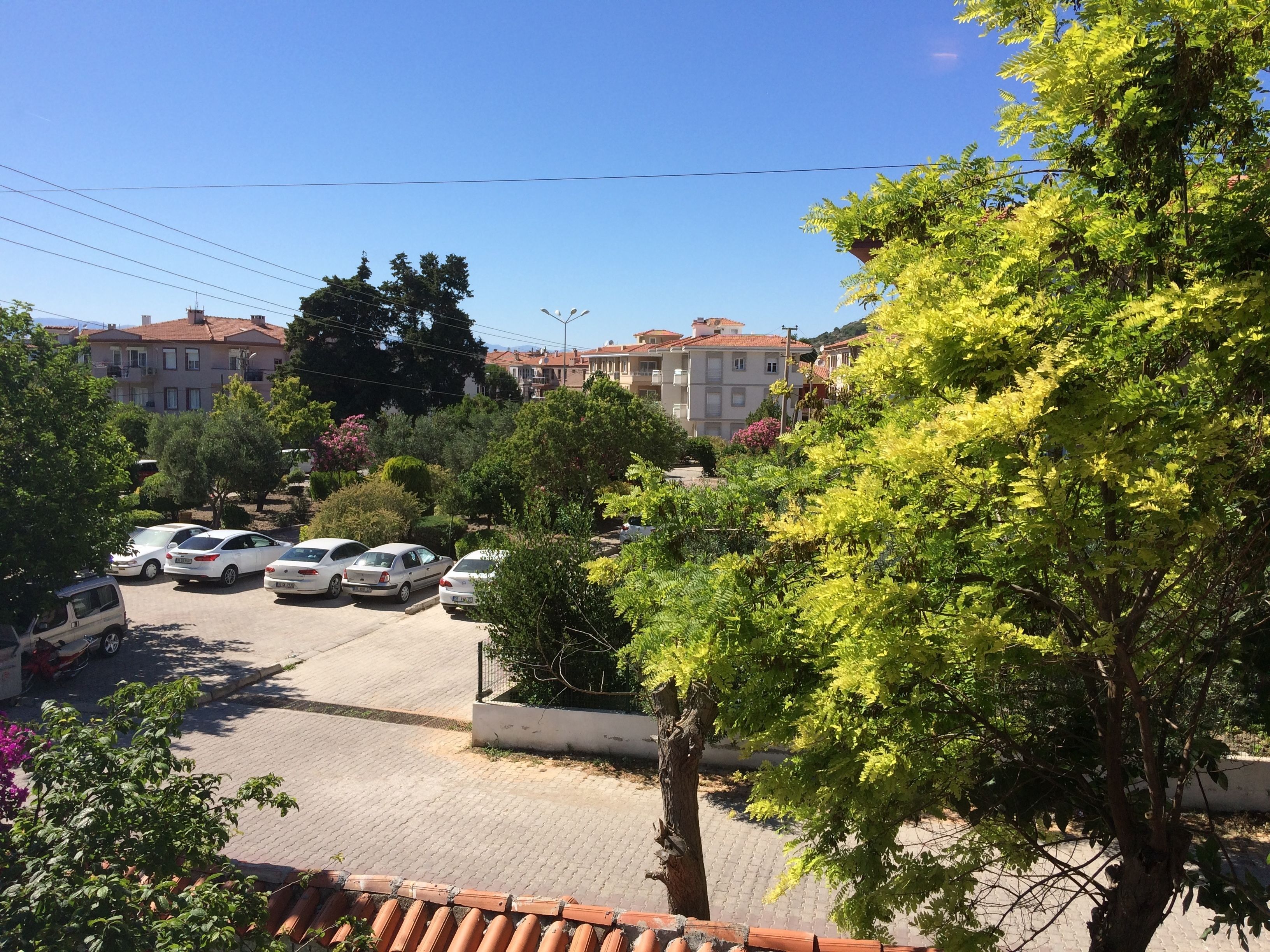 Um estacionamento com vários carros, cercado por árvores e edifícios com telhados de telha vermelha.