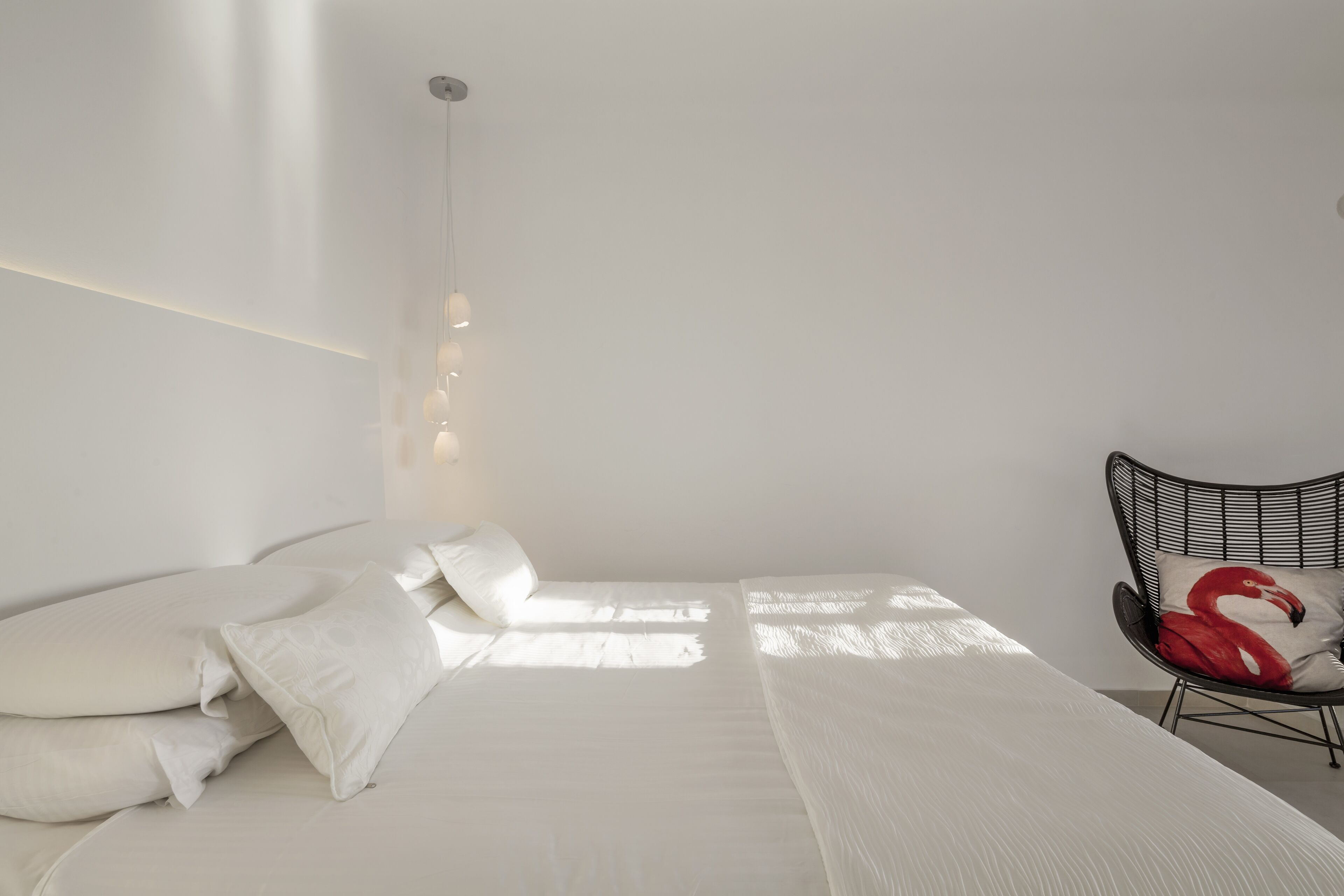 Quarto minimalista com cama, almofadas, uma cadeira com almofada de flamingo e um pendente.