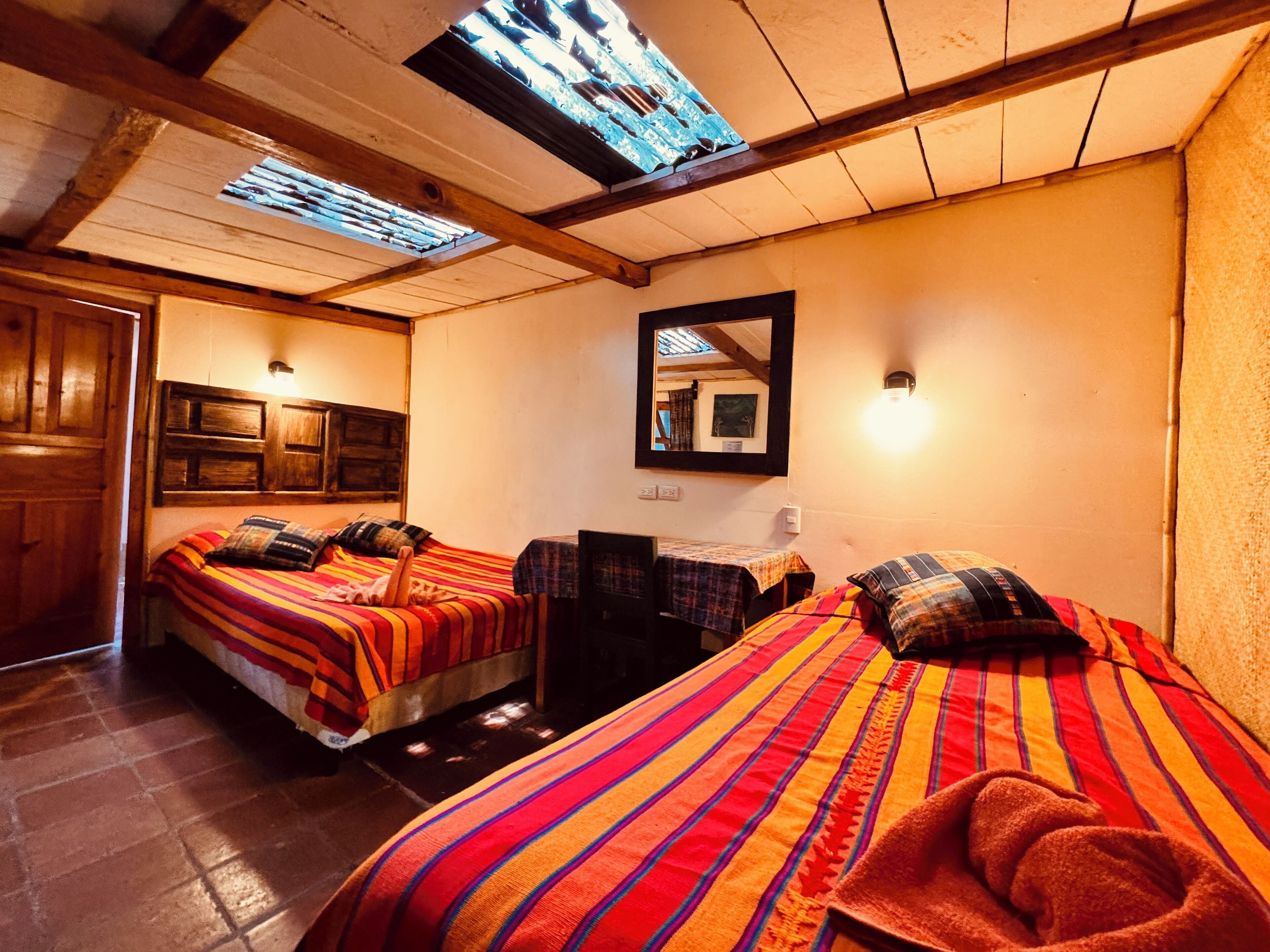 Quarto com duas camas, vigas de madeira no teto, um espelho e uma mesa pequena.