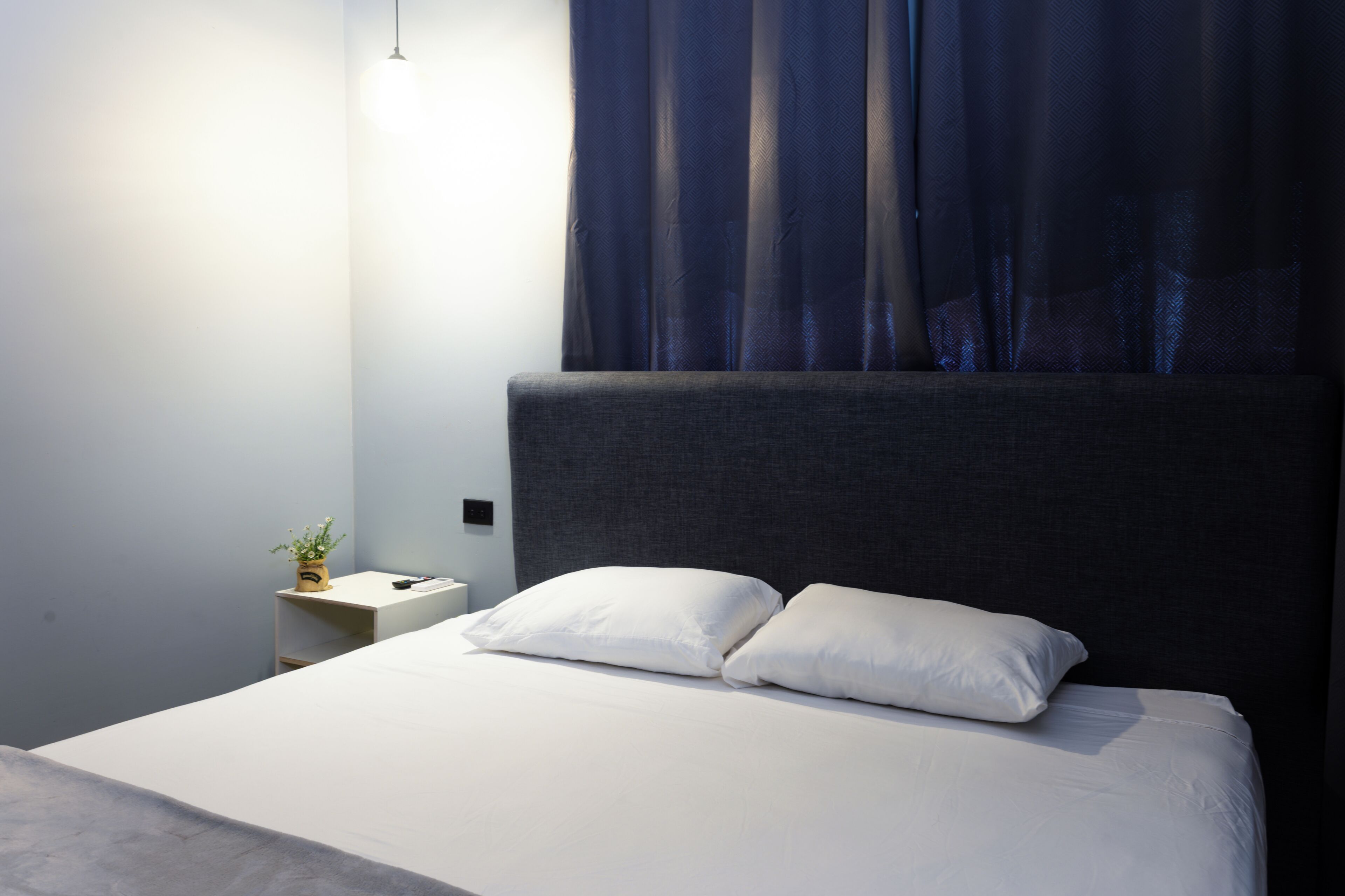 Quarto de hotel com uma cama grande, uma mesa de cabeceira, um abajur e uma janela com cortinas.