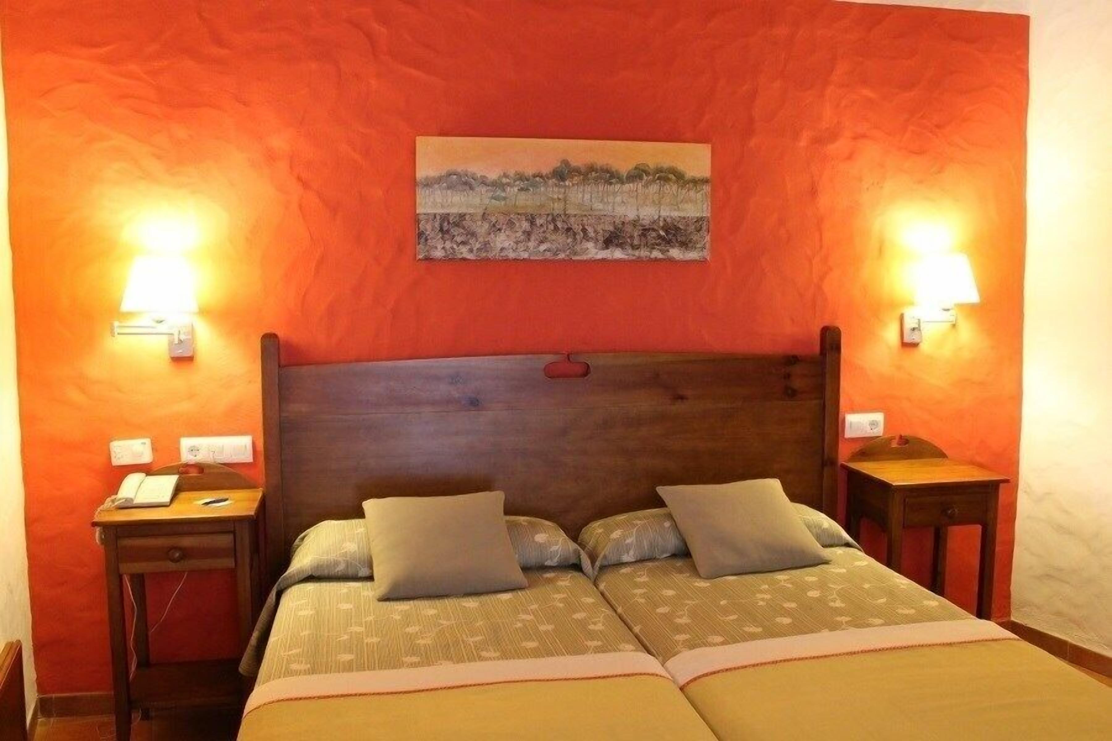 Uma cama de casal com duas almofadas, uma cabeceira de madeira e duas mesas de cabeceira com abajures.