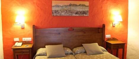 Uma cama de casal com duas almofadas, uma cabeceira de madeira e duas mesas de cabeceira com abajures.