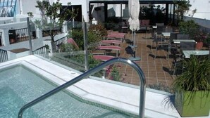 Área de piscina com escada de metal, cercada por assentos externos e vasos de plantas.