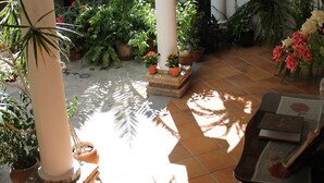Um pátio interno com arcos, plantas em vasos e uma mesa com livros.