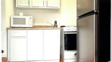 Cozinha compacta com armários brancos, geladeira de aço inoxidável, micro-ondas e forno.