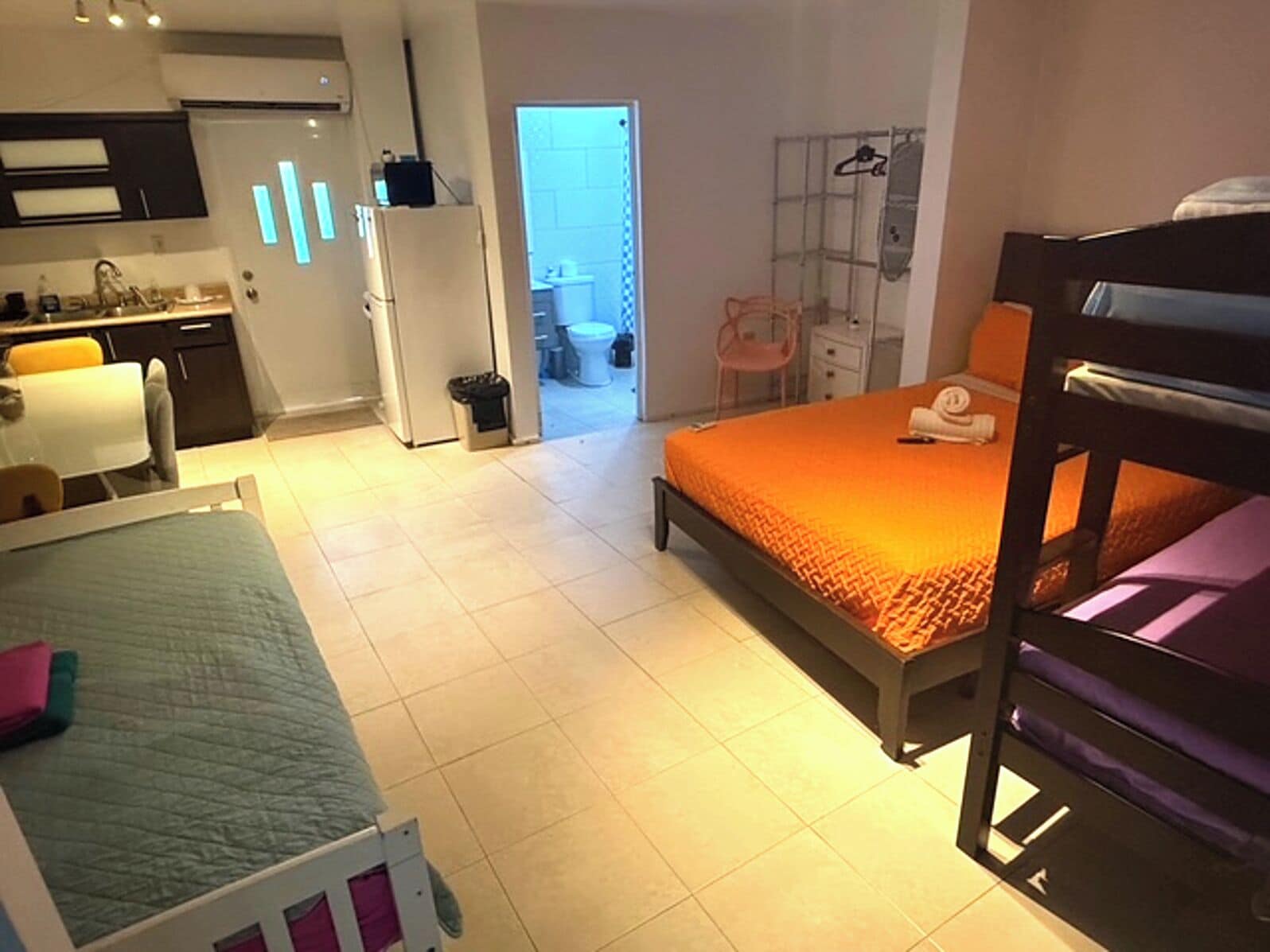 Quarto com cama de solteiro, beliche, cozinha compacta, banheiro e área de chuveiro.