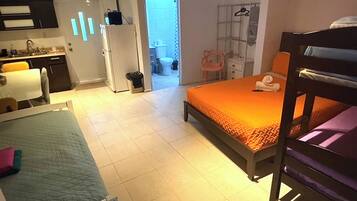 Quarto com cama de solteiro, beliche, cozinha compacta, banheiro e área de chuveiro.