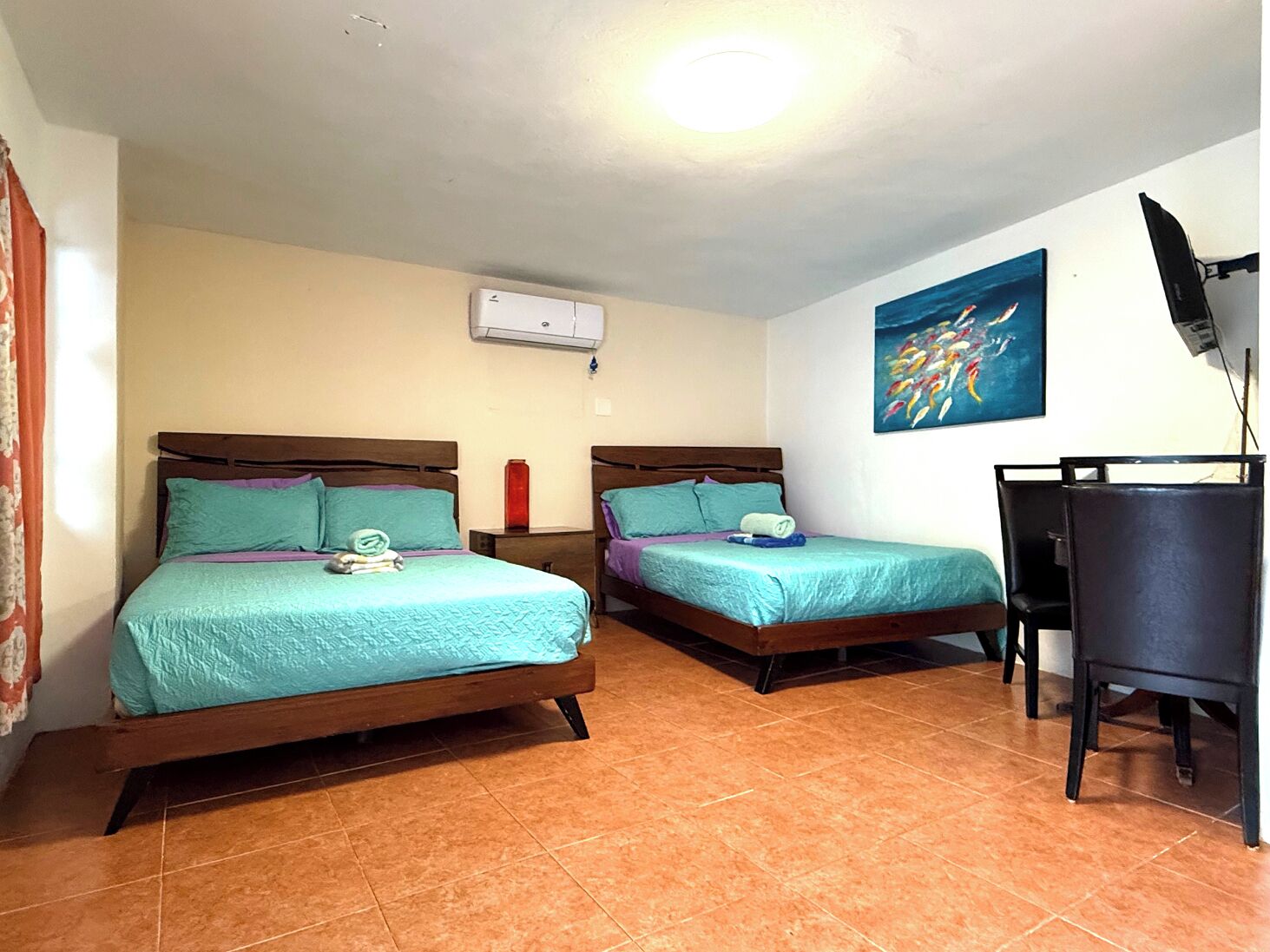 Quarto com duas camas, uma escrivaninha, ar condicionado e um quadro na parede.