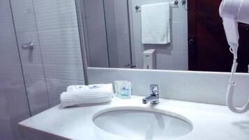 Casa de banho com lavatório branco, espelho, porta-toalhas e secador de cabelo.